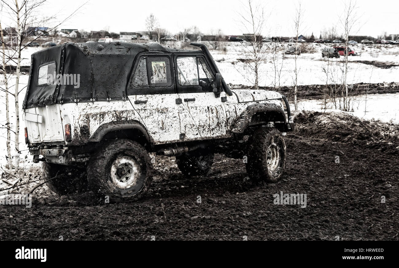 The car rides on a rough road in the winter, all stained with mud from ...