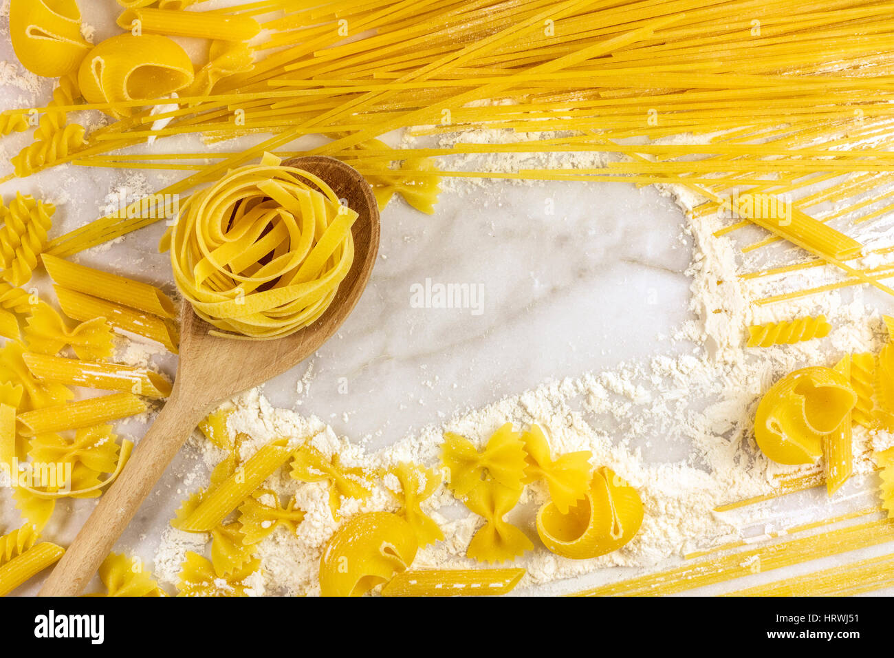 Various types of pasta on a white marble table with flour, forming a ...