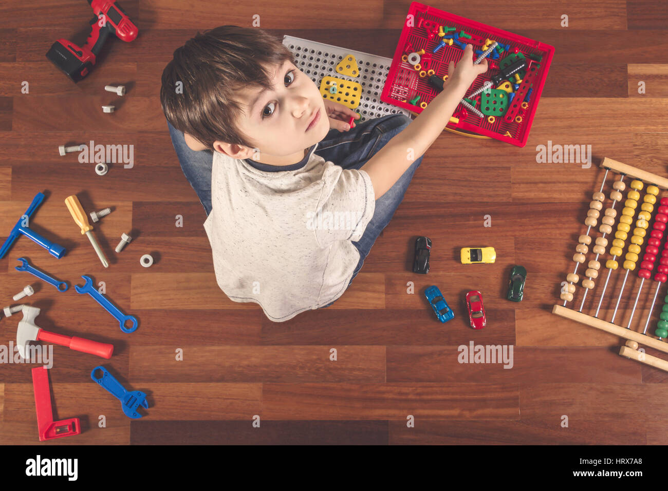 Kid playing with different toys while sitting on wooden floor in his ...