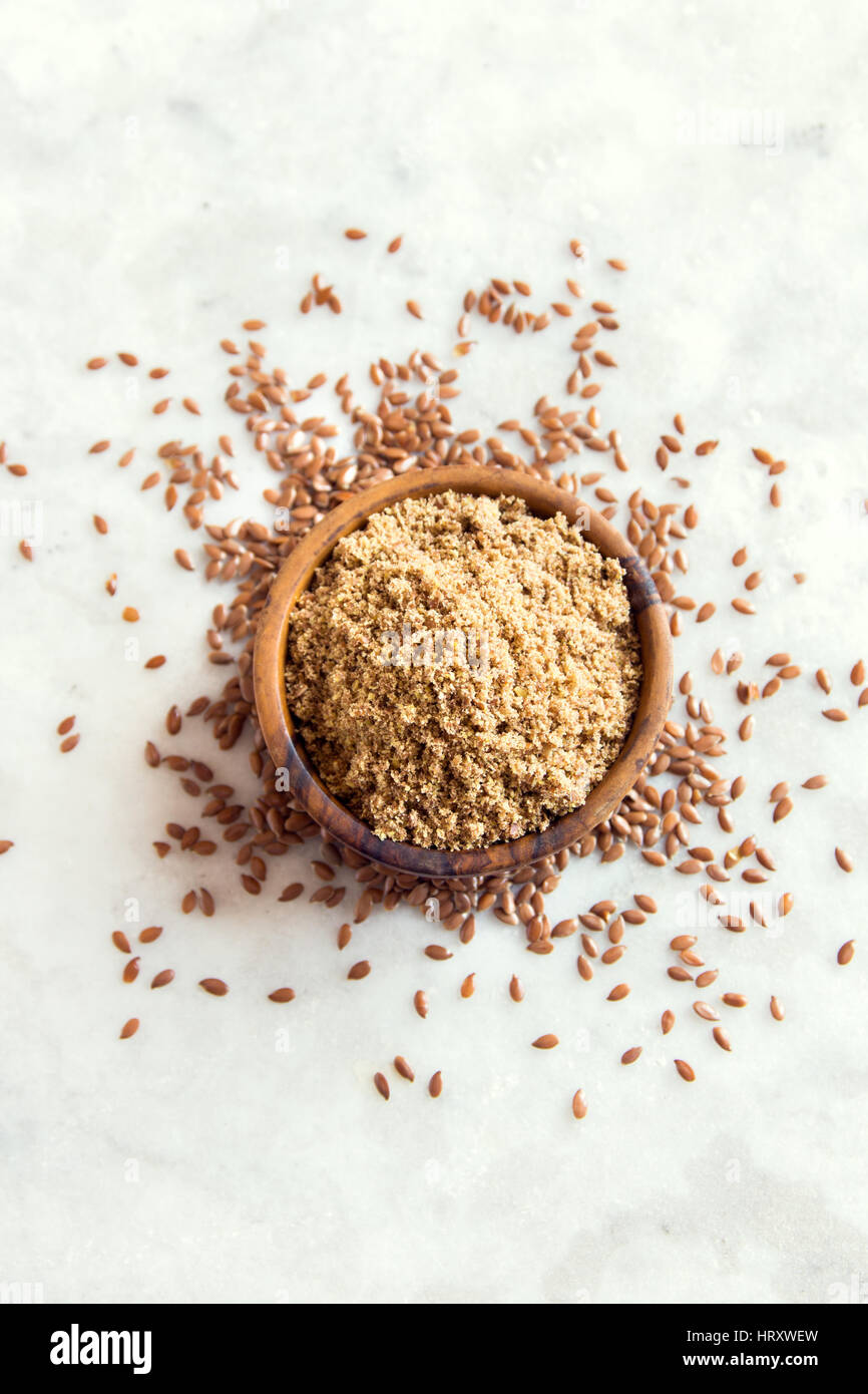 Crushed flax seeds (ground linseed) on wooden spoon and white stone table - healthy organic ...