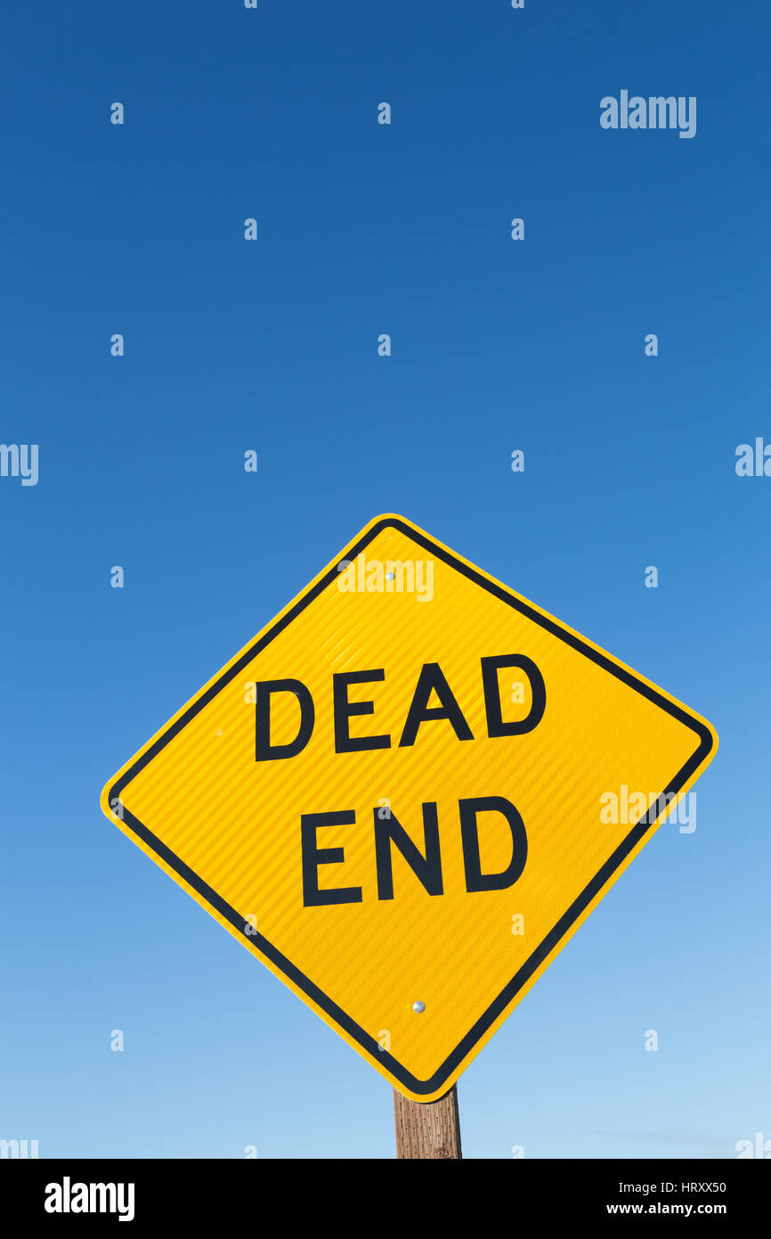 Yellow and black dead end street sign against a vivid blue sky ...