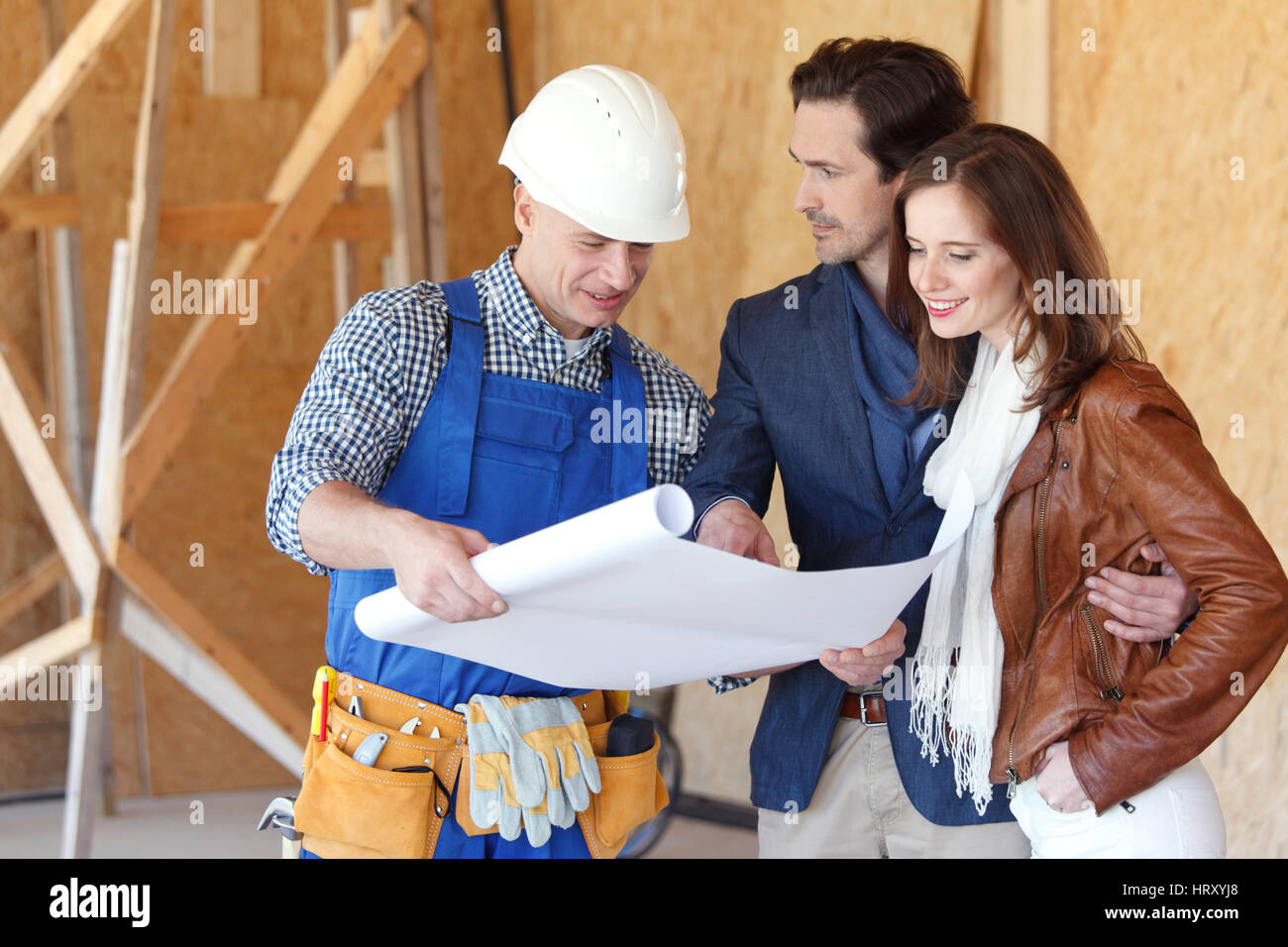 Worker shows house design plans to a young couple at construction site ...