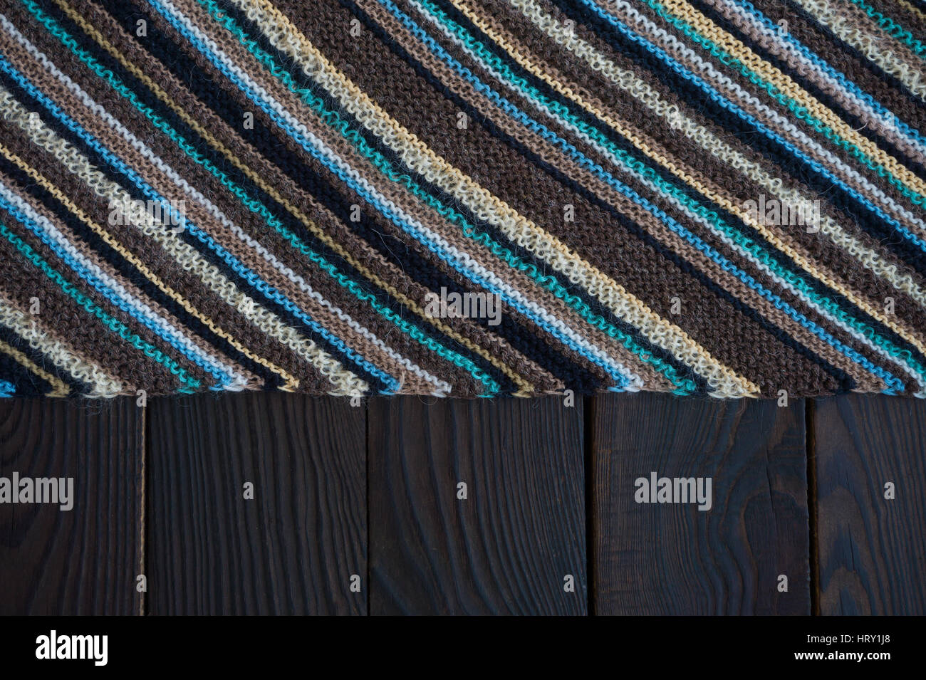 Knitted fabric fragment handmade with strips on a dark wooden surface ...