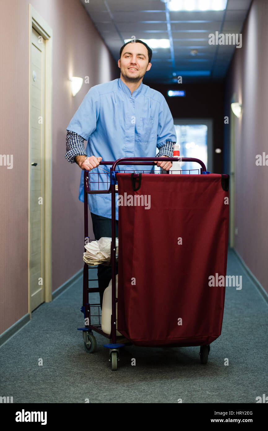 Young man pushing a housekeeping cart laden with clean towels, laundry ...