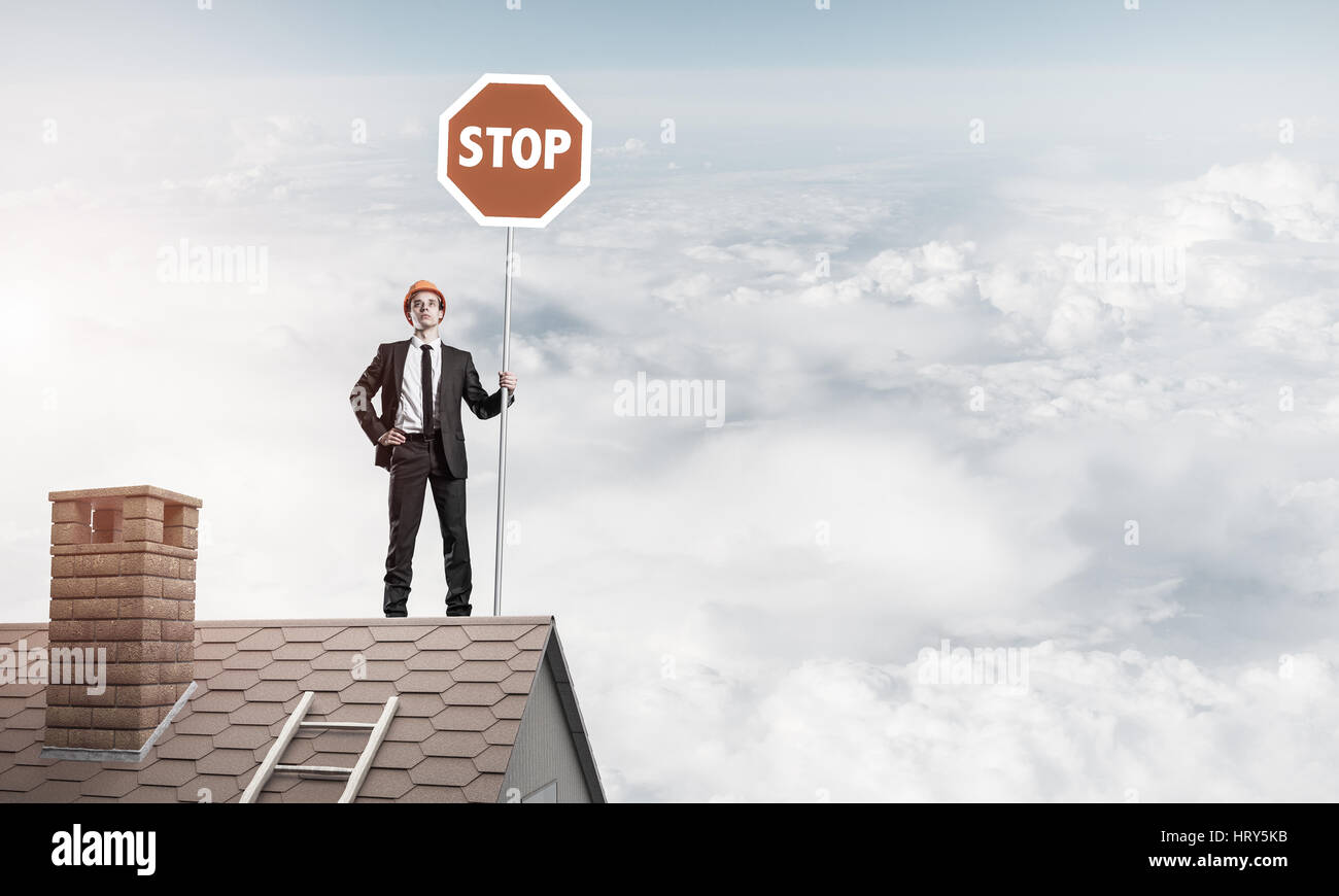 Engineer man standing on house roof and holding red prohibition sign ...