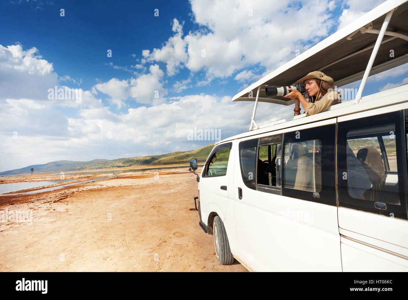Young woman standing in open roof of safari minibus and taking pictures ...