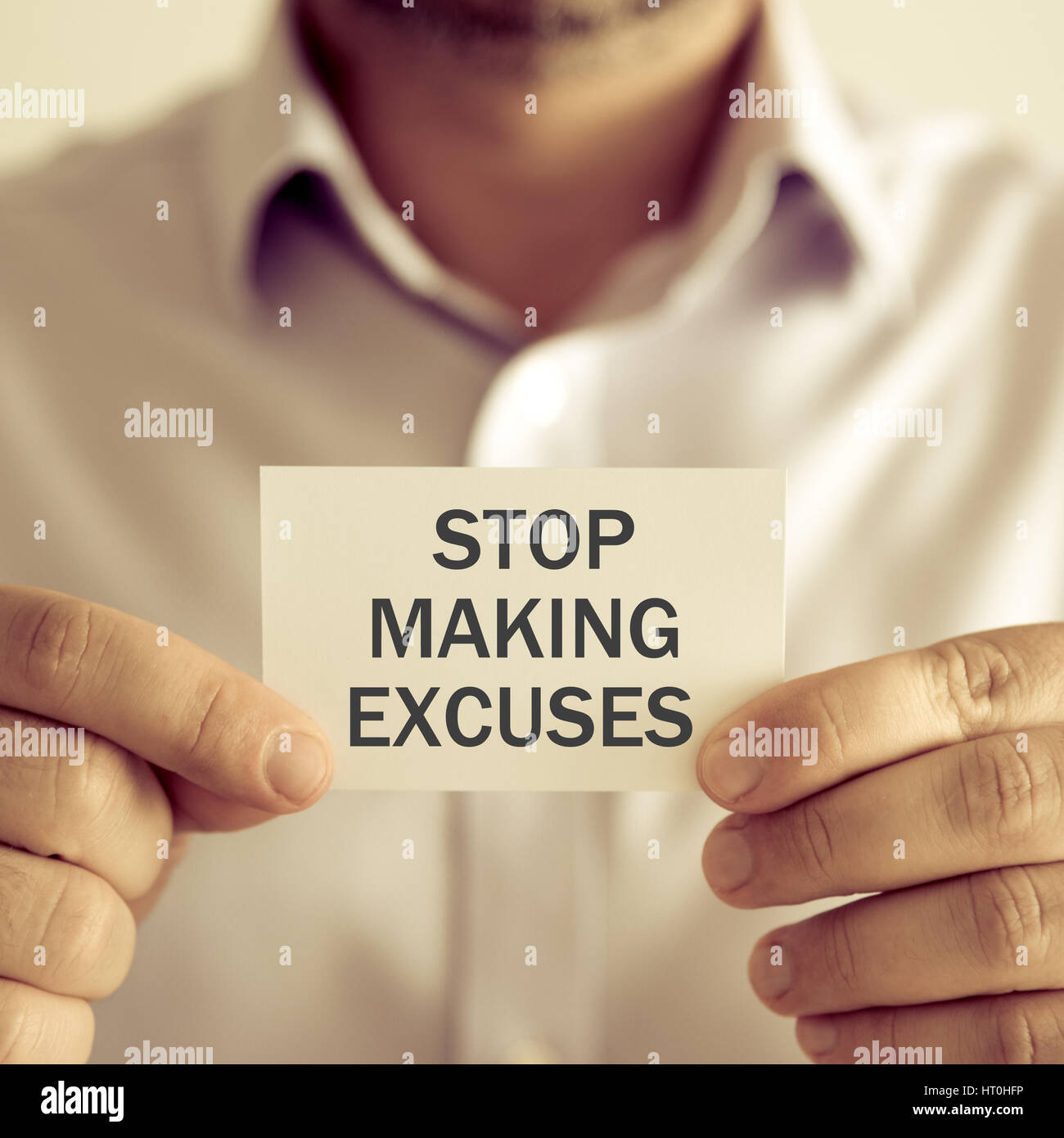 Closeup on businessman holding a card with text STOP MAKING EXCUSES ...