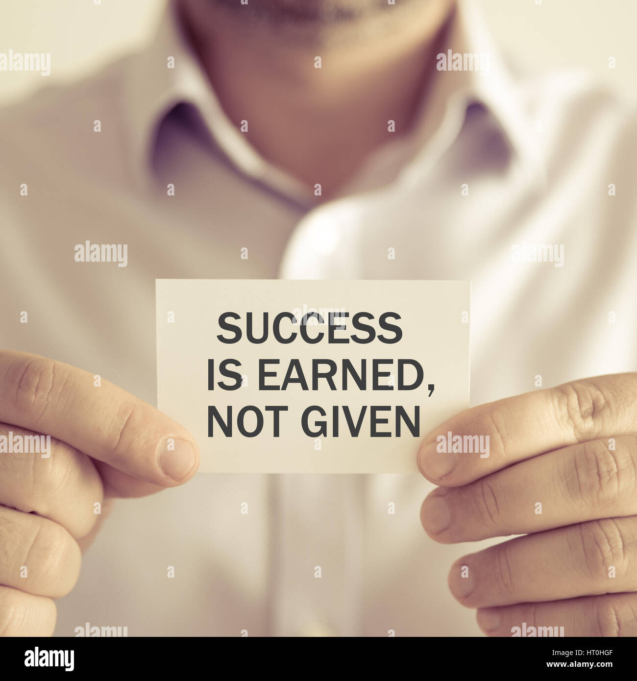 Closeup on businessman holding a card with text SUCCESS IS EARNED, NOT ...