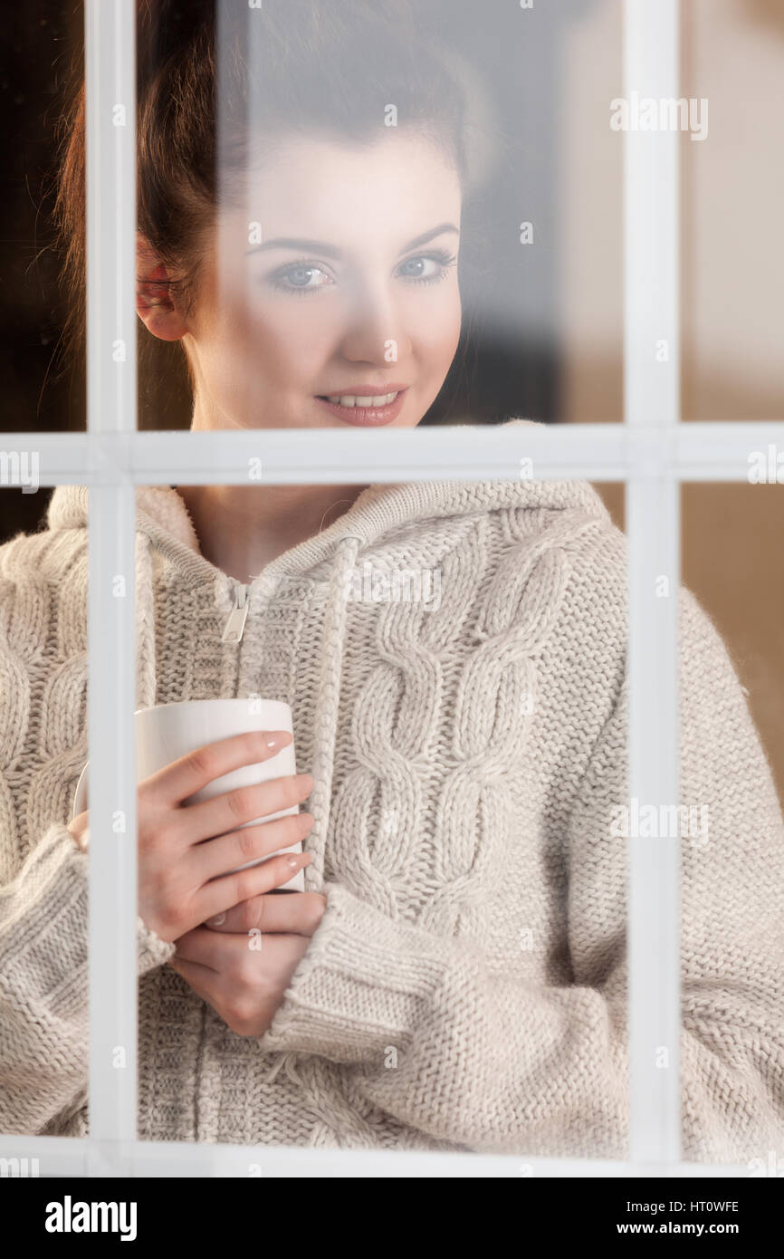 Beautiful woman drinking hot drink standing by the window. View from ...