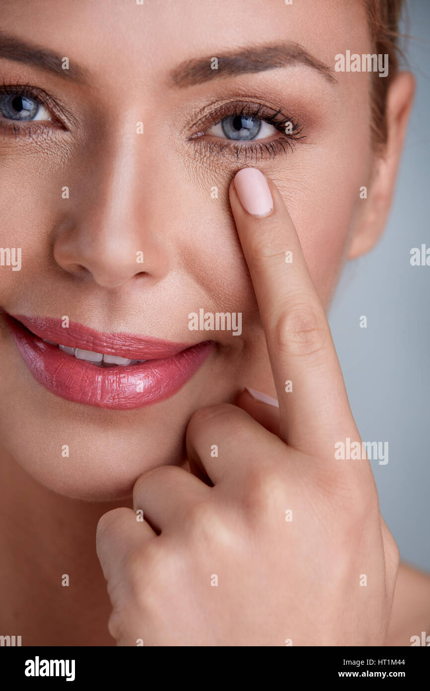Woman holding finger on skin under eyes, checking wrinkles Stock Photo ...