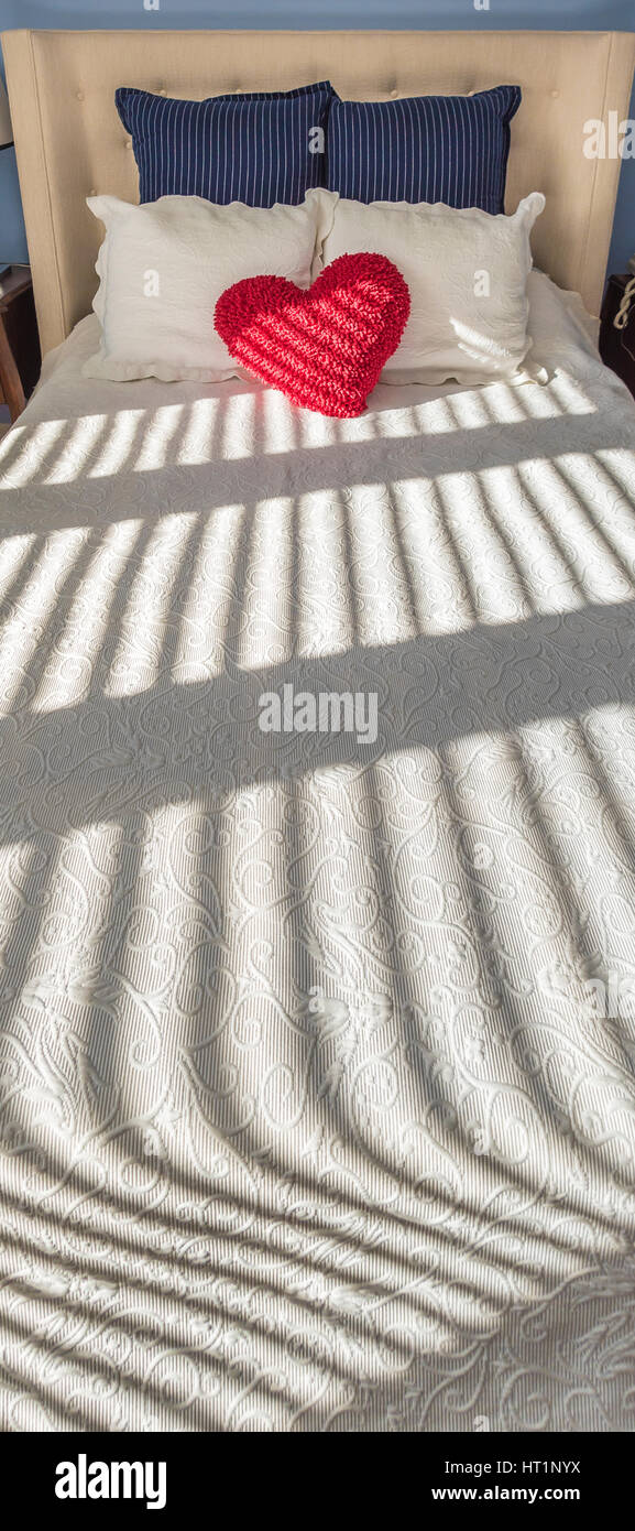 A bed sun drenched with light through blinds cast a linear shadow on a ...