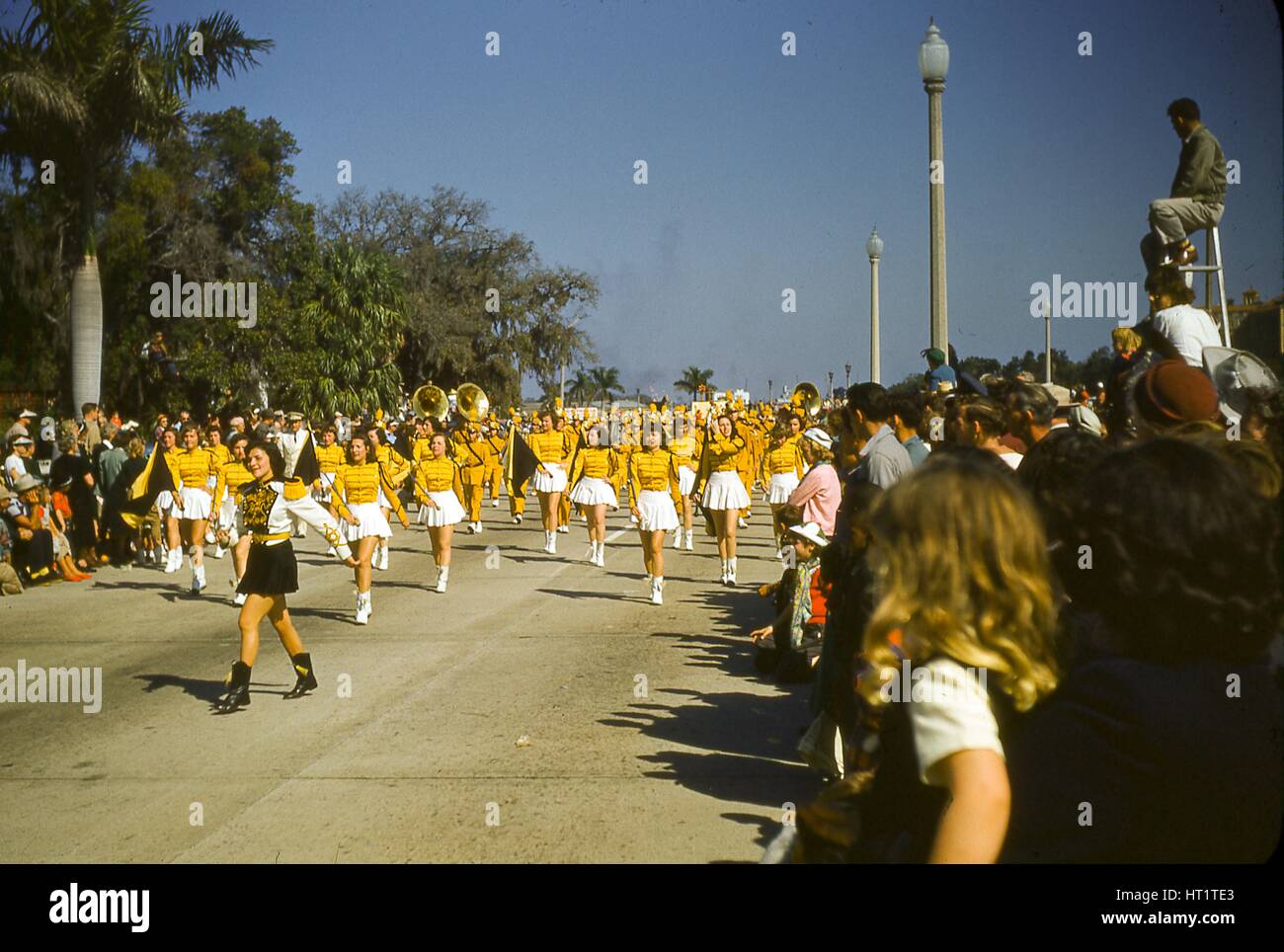 A marching band in yellow uniforms parades down a city street in Saint ...