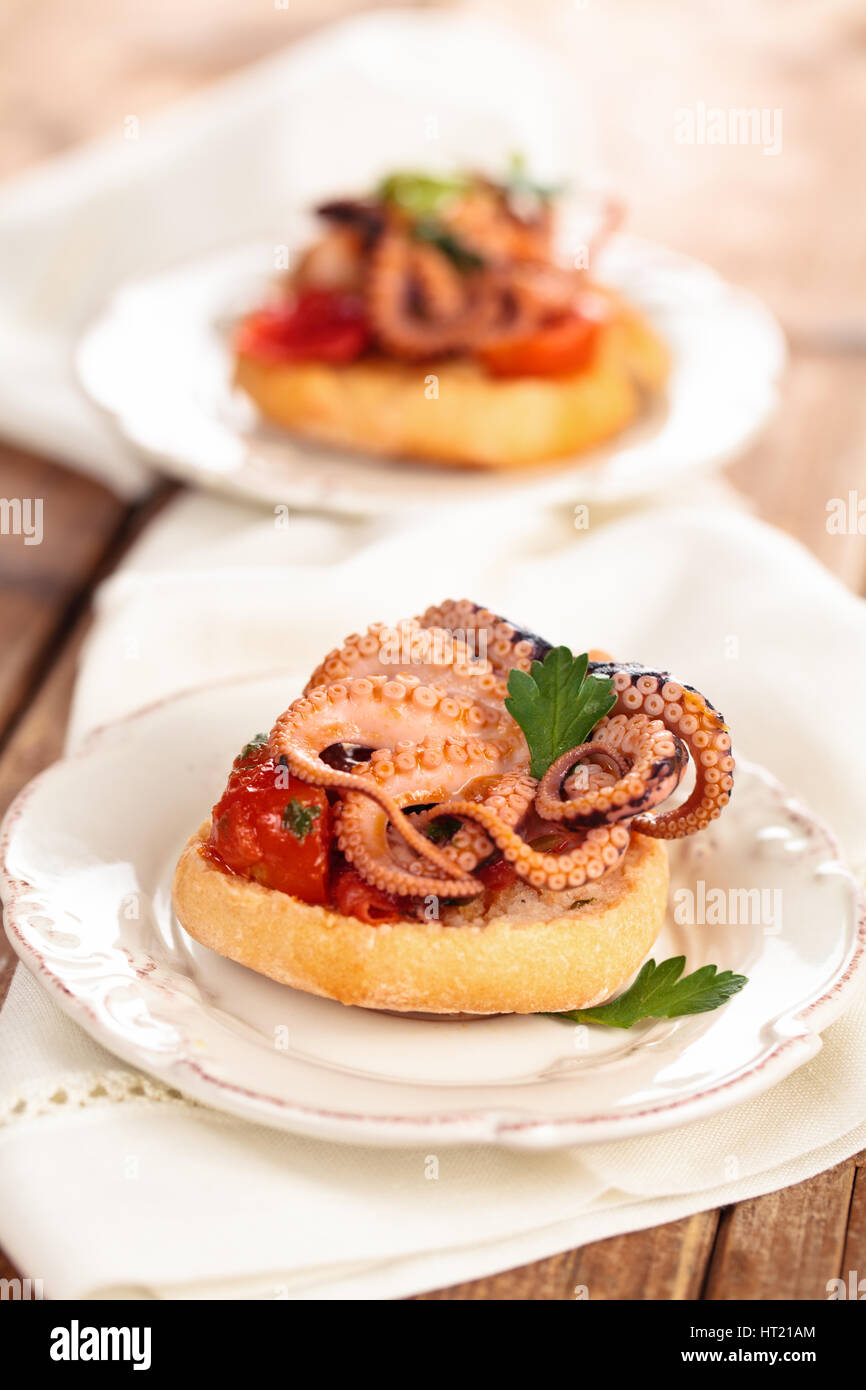Italian food. Bruschetta with baby octopuses, tomatoes and parsley ...