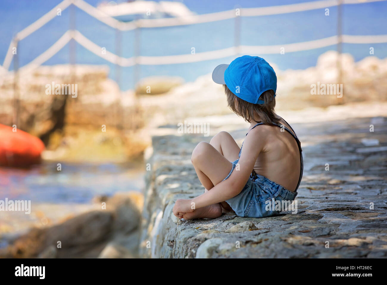 Cute boy, sitting on a pier in Mediterranean sea on French riviera ...
