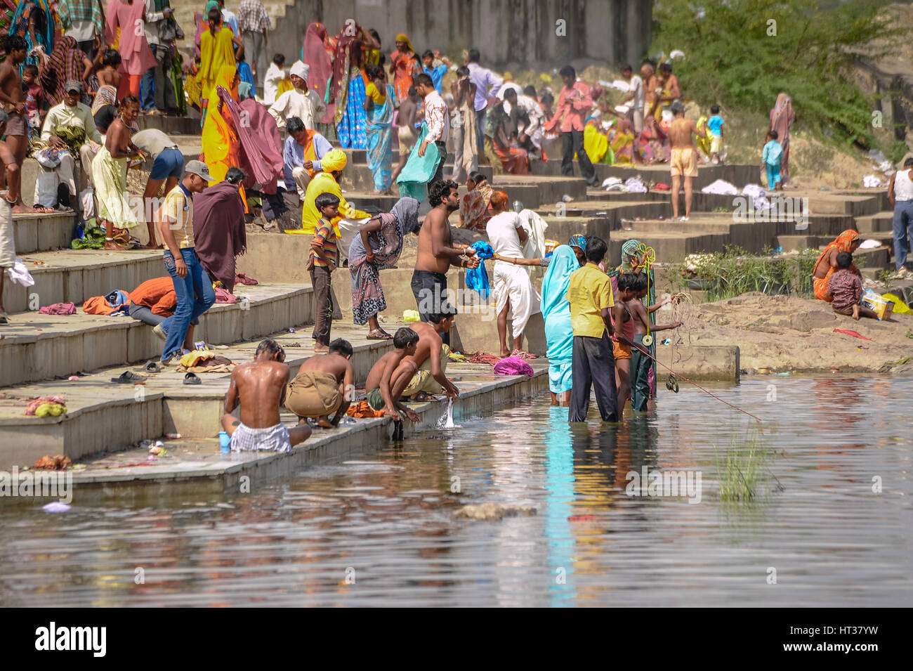 A group of people wash their clothes on steps by a river in rural ...
