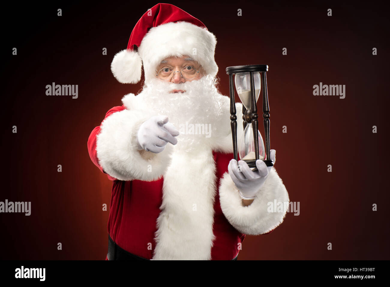 Santa Claus with hourglass pointing at camera Stock Photo - Alamy