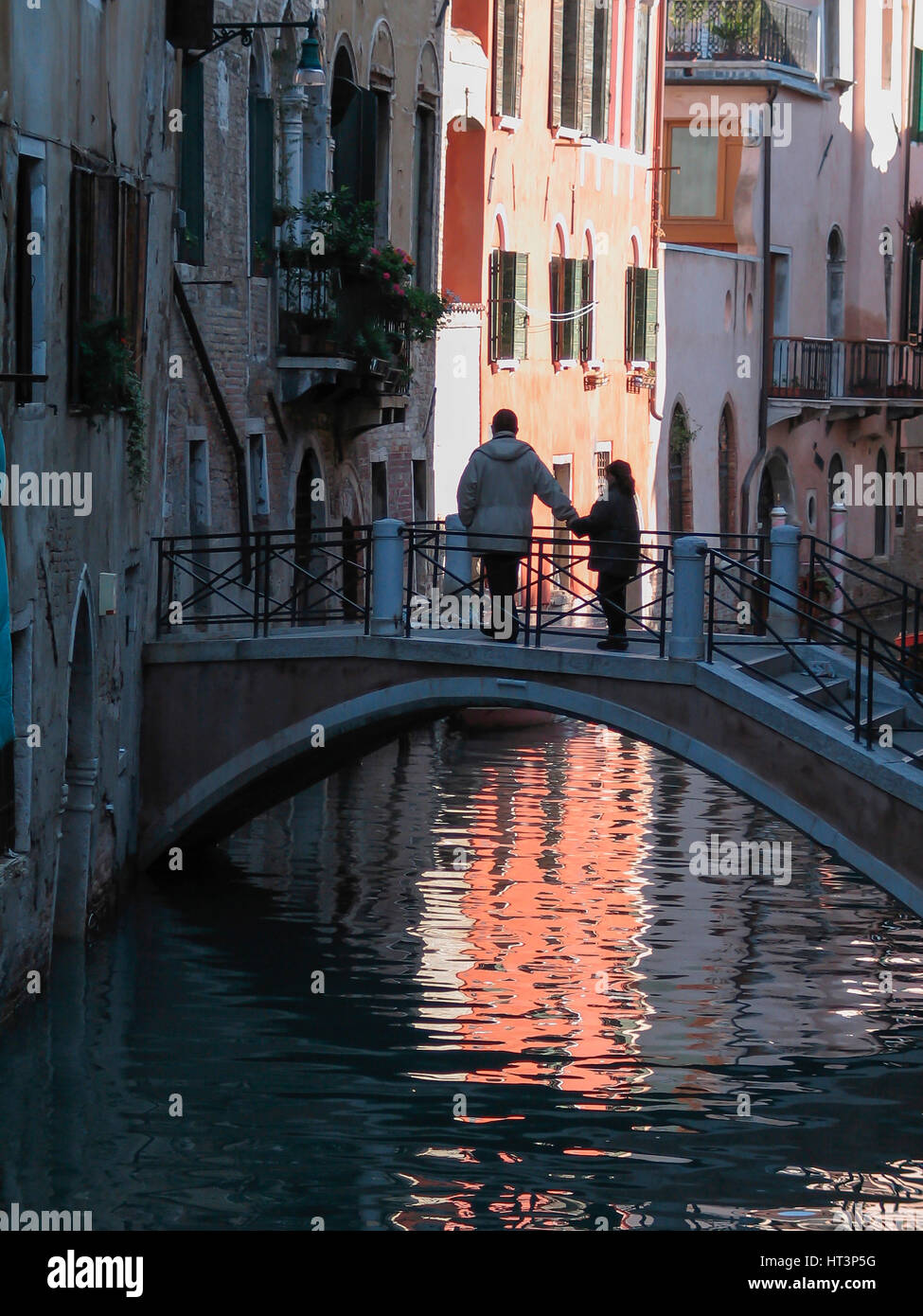Couple holding hands on a bridge above a serene canal in Venice during ...