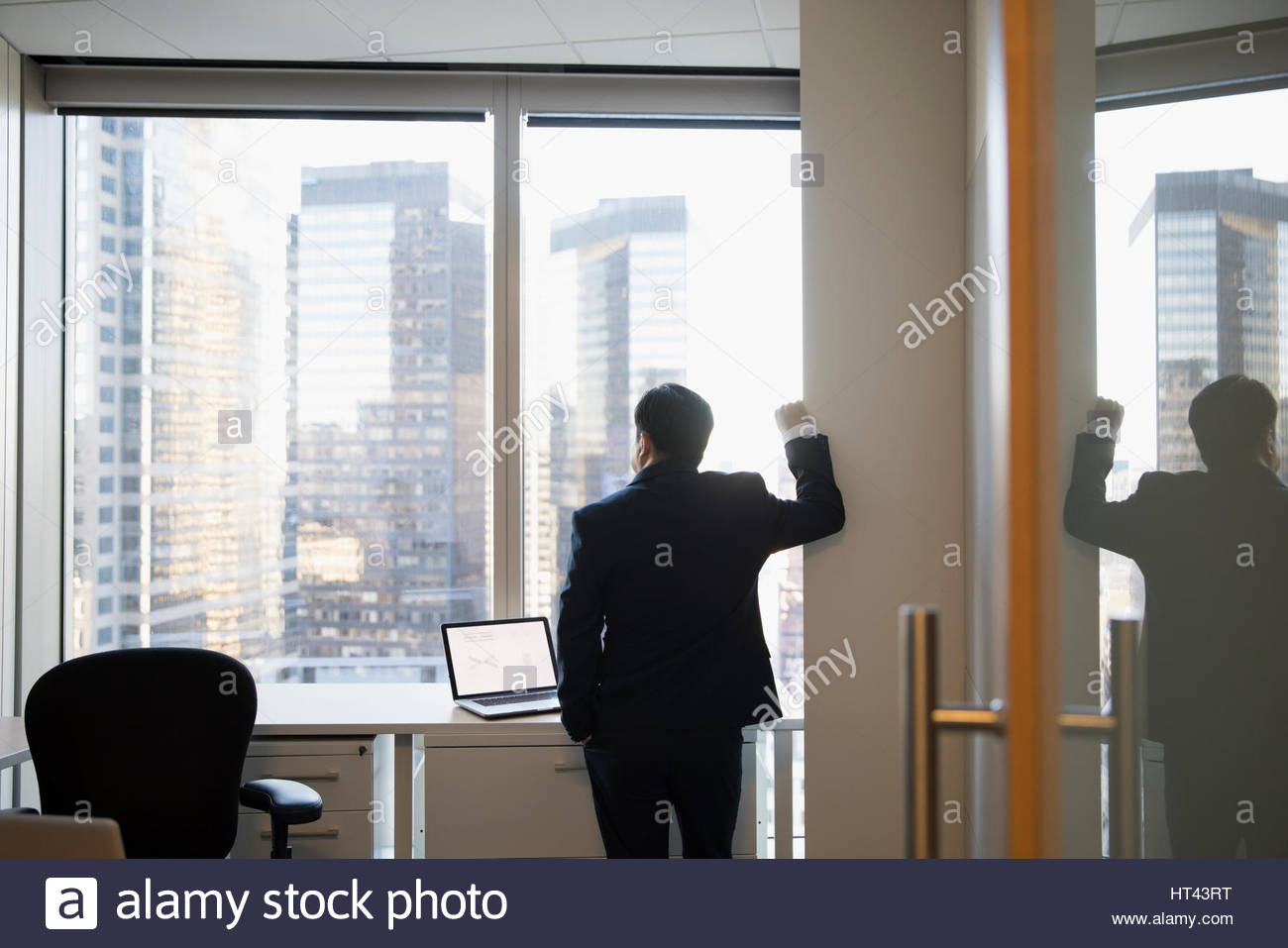 Pensive businessman looking out office windows at highrise buildings ...