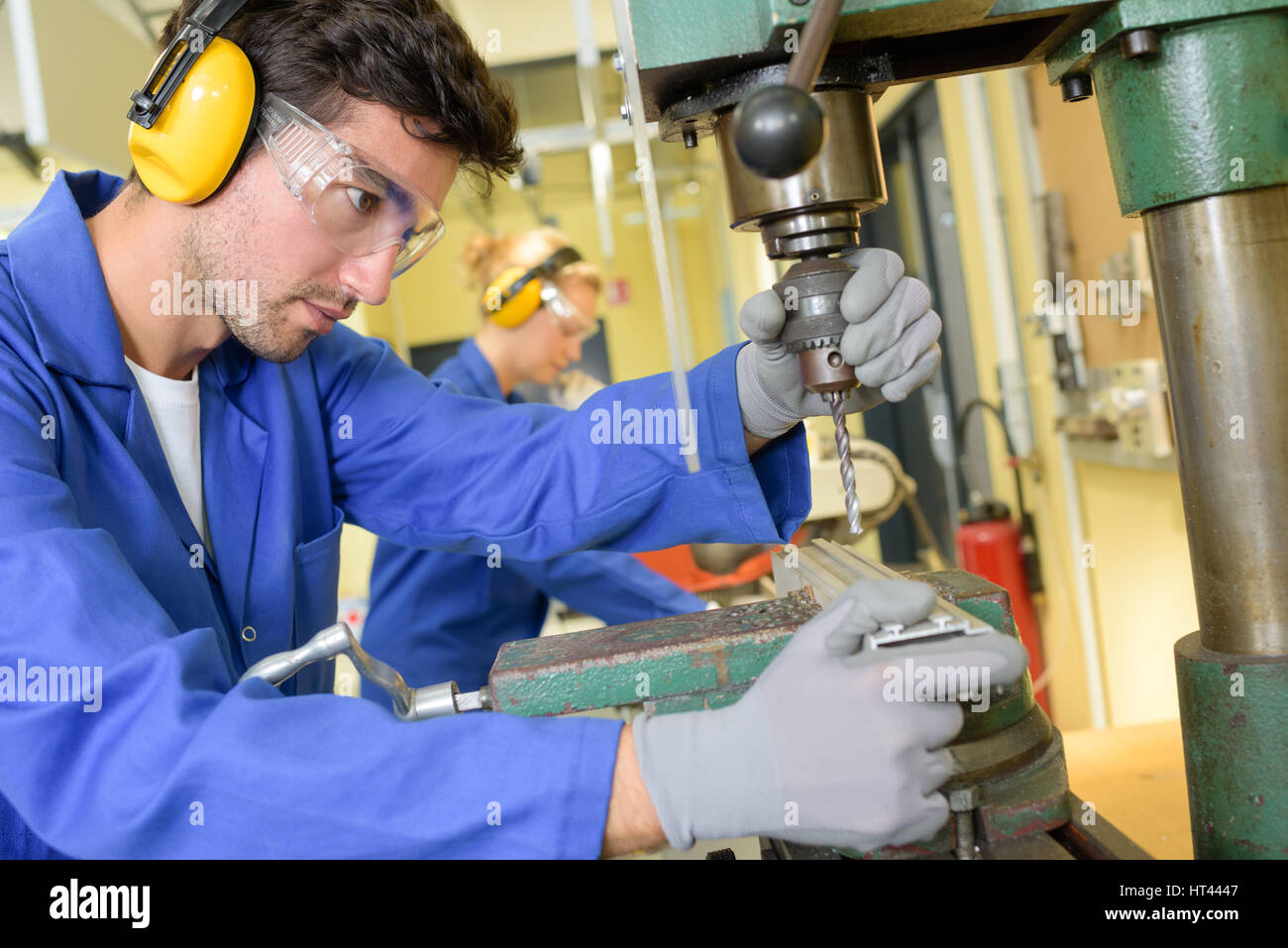 serious trainees focused on drilling metal piece with professional ...