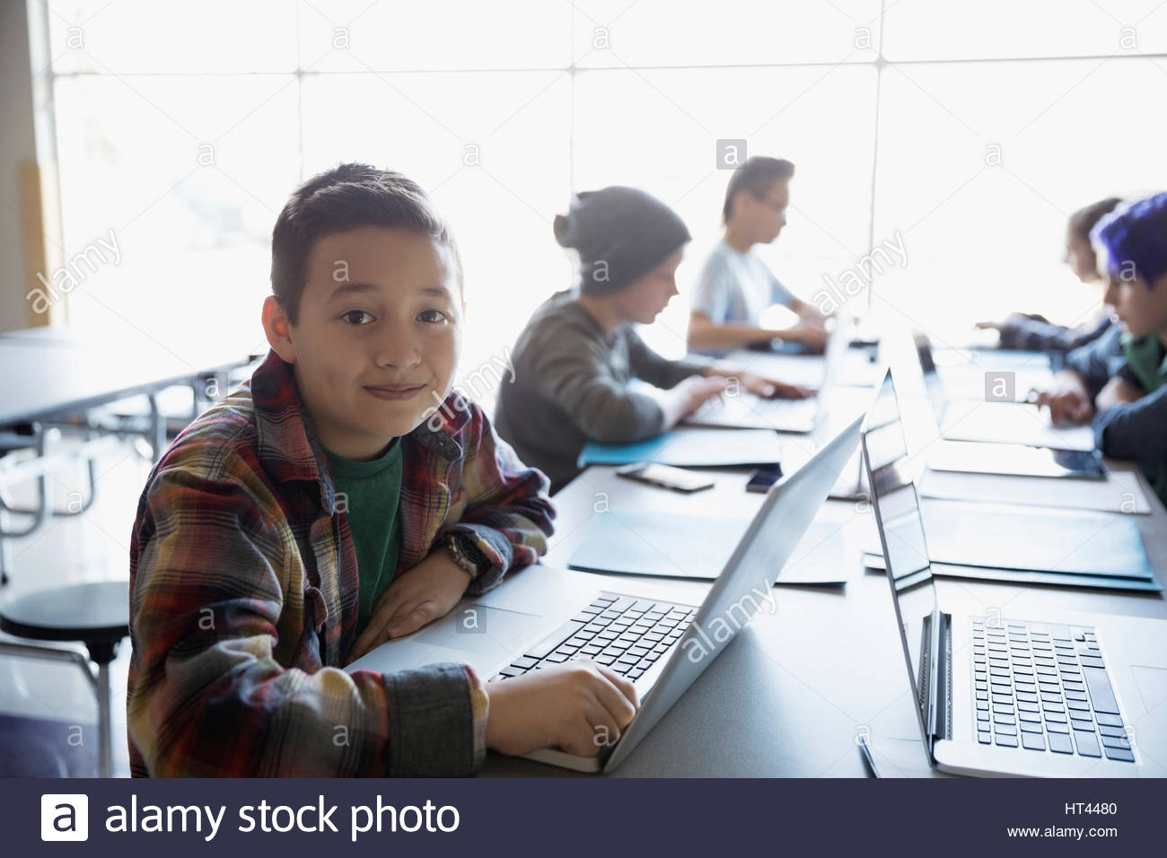 Portrait confident pre-adolescent boy studying at laptop in classroom ...