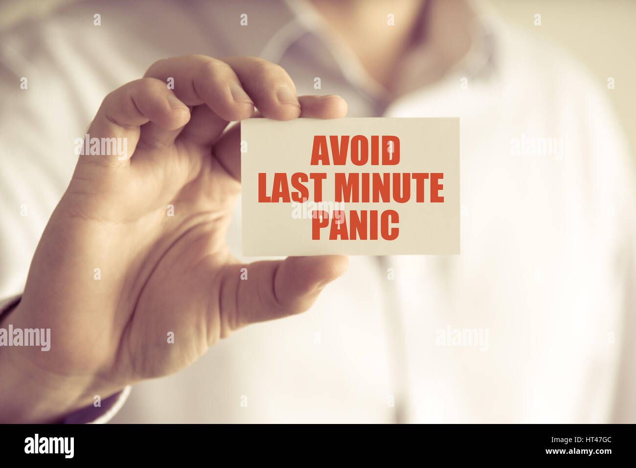Closeup on businessman holding a card with text AVOID LAST MINUTE PANIC ...