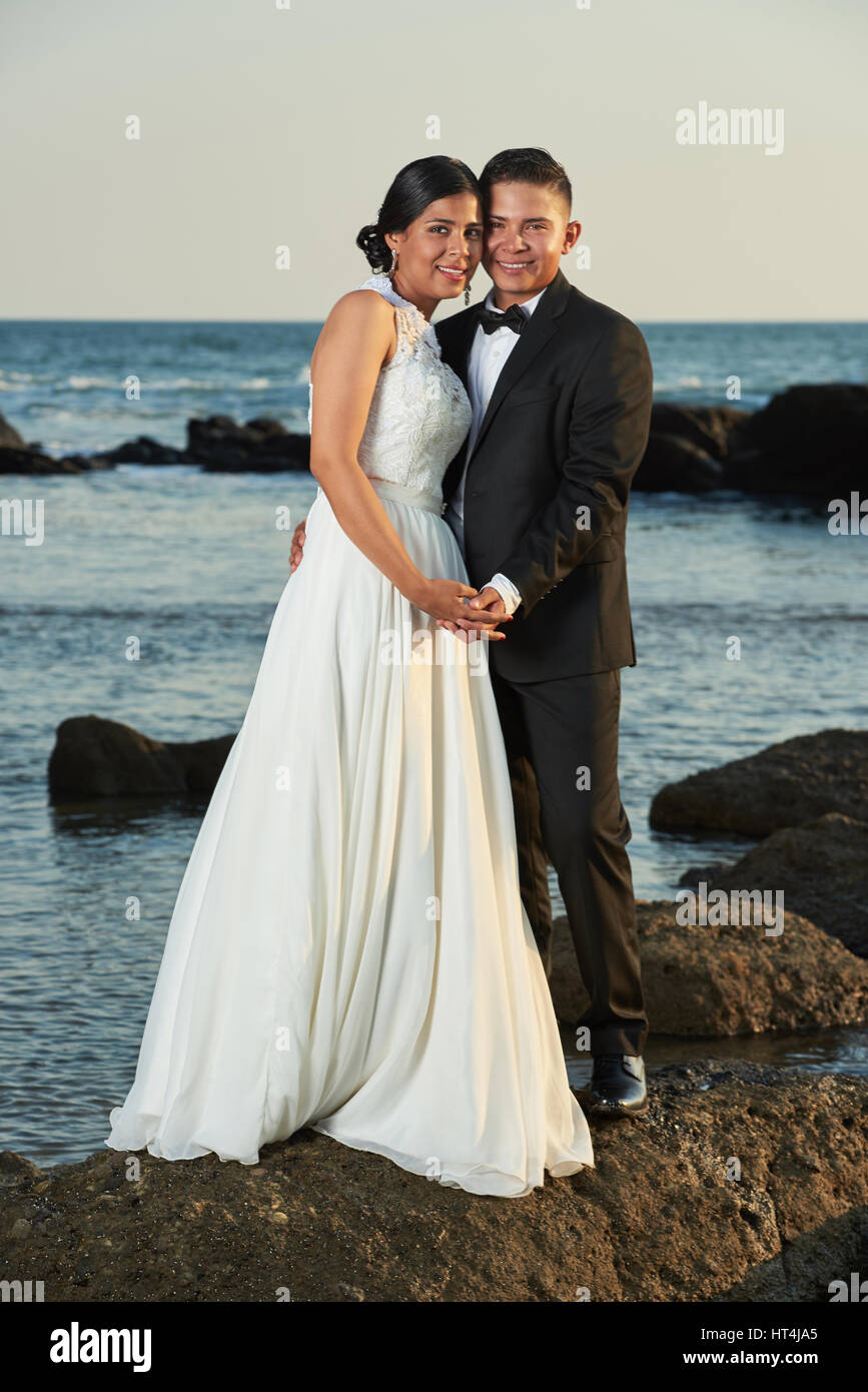 Wedding on ocean coast of hispanic couple. Young bride and groom stand ...