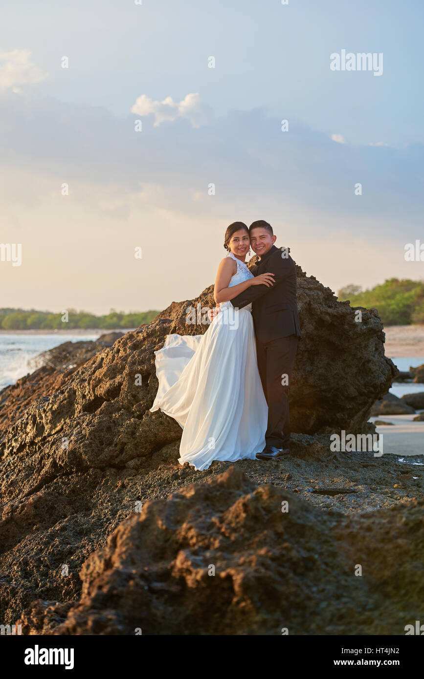 Hugging bride and groom standing on rock at sunny sunset time with copy ...