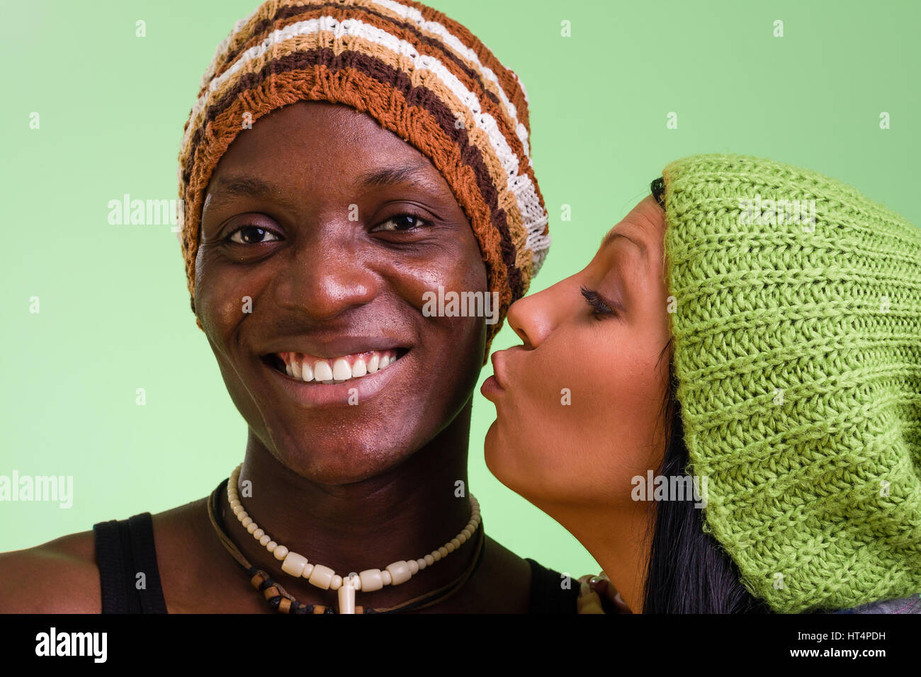 Attractive couple in winter fashion cap smiling at camera on green ...