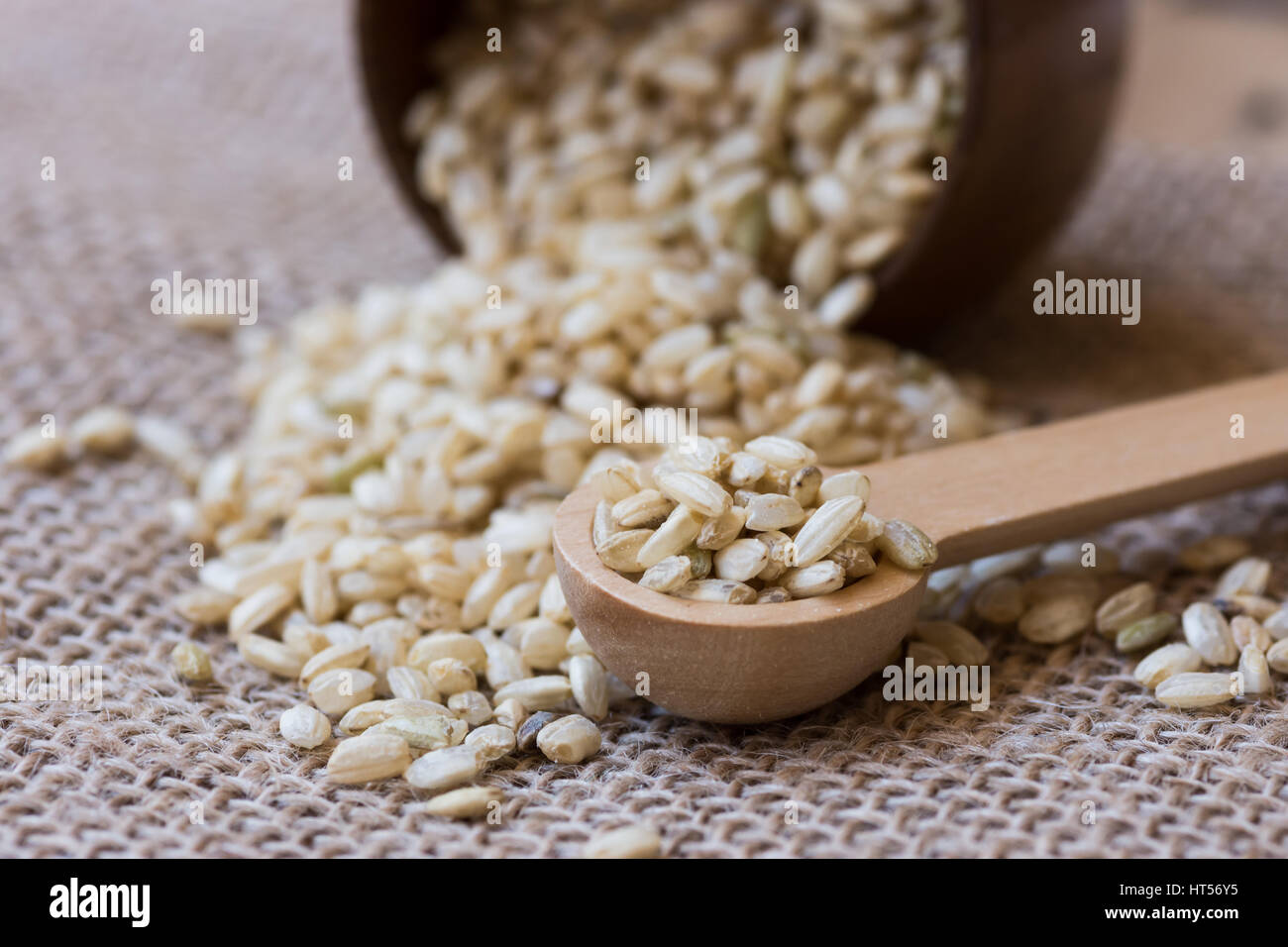 Spilled grains of brown rice scattered over sackcloth, wooden bowl and ...