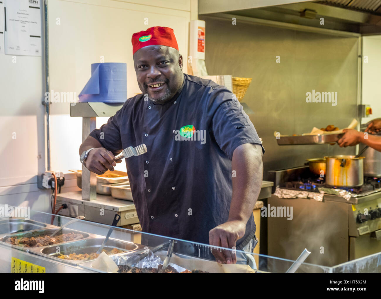 Afro- Caribbean Chef leaning over the serving counter in his kitchen ...