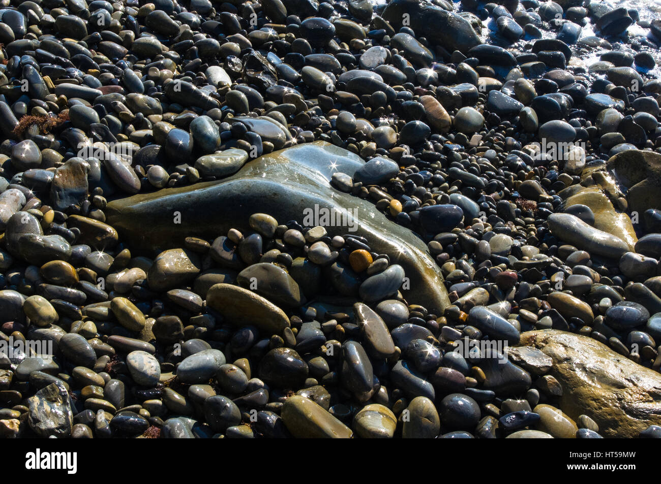 sea pebble beach with multicoloured stones, transparent waves with foam ...