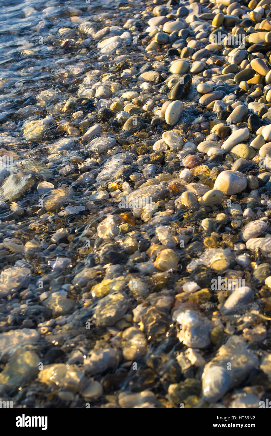 sea pebble beach with multicoloured stones, transparent waves with foam ...