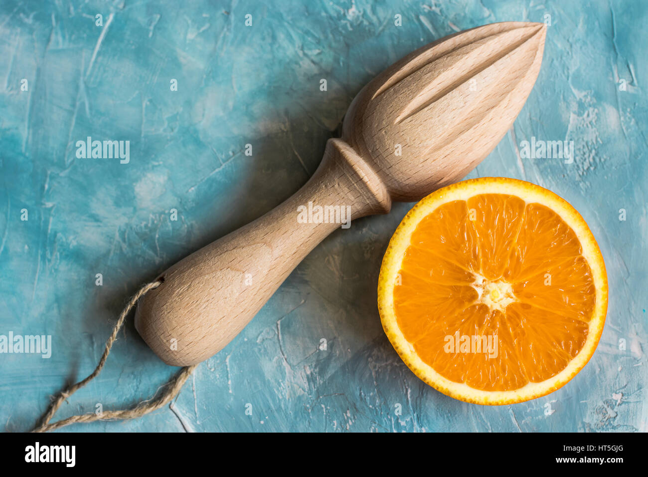 Juicy ripe fresh orange cut in half with wooden reamer on blue concrete ...