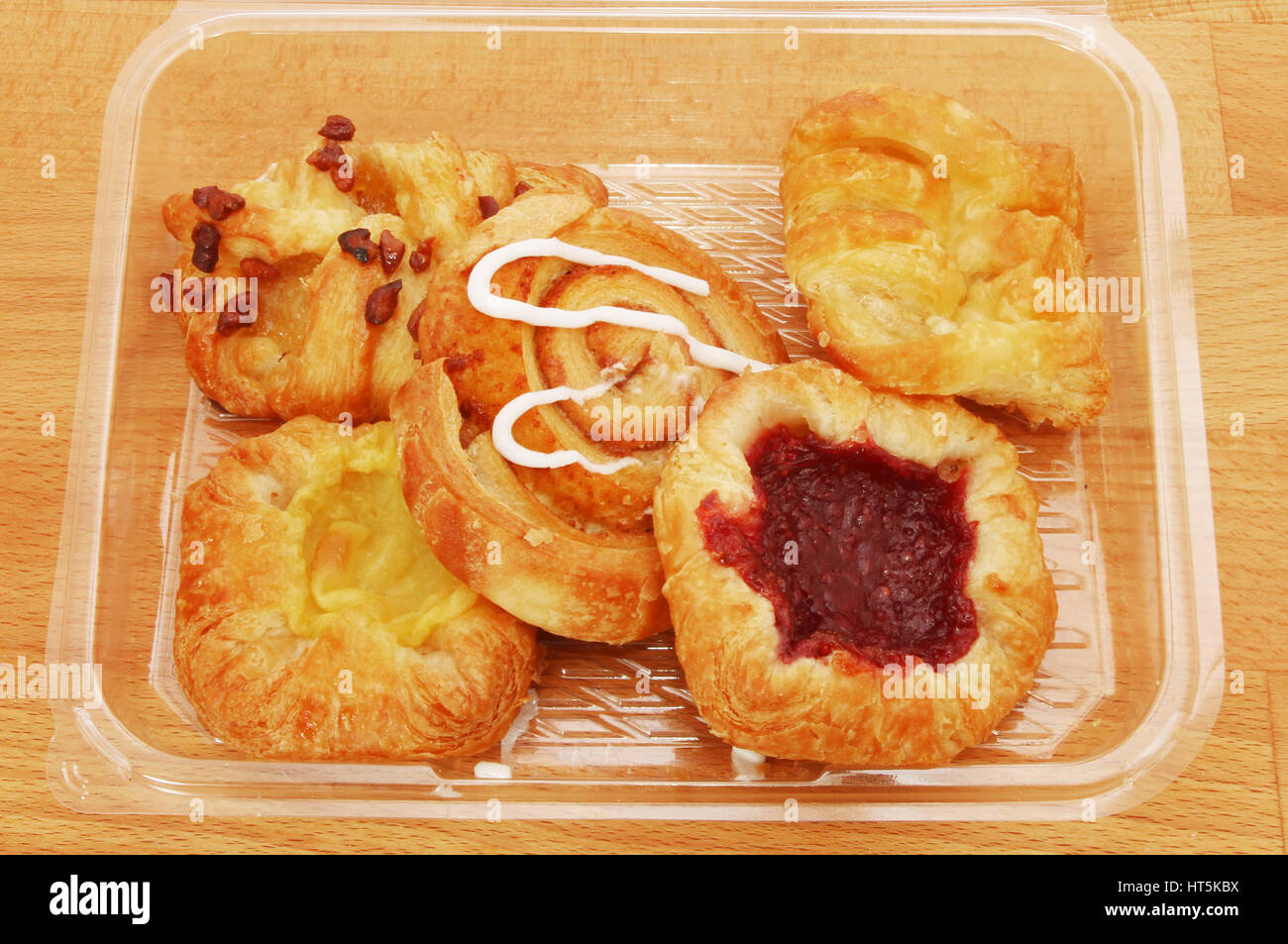 Selection of Danish pastries in a plastic carton on a wooden tabletop ...