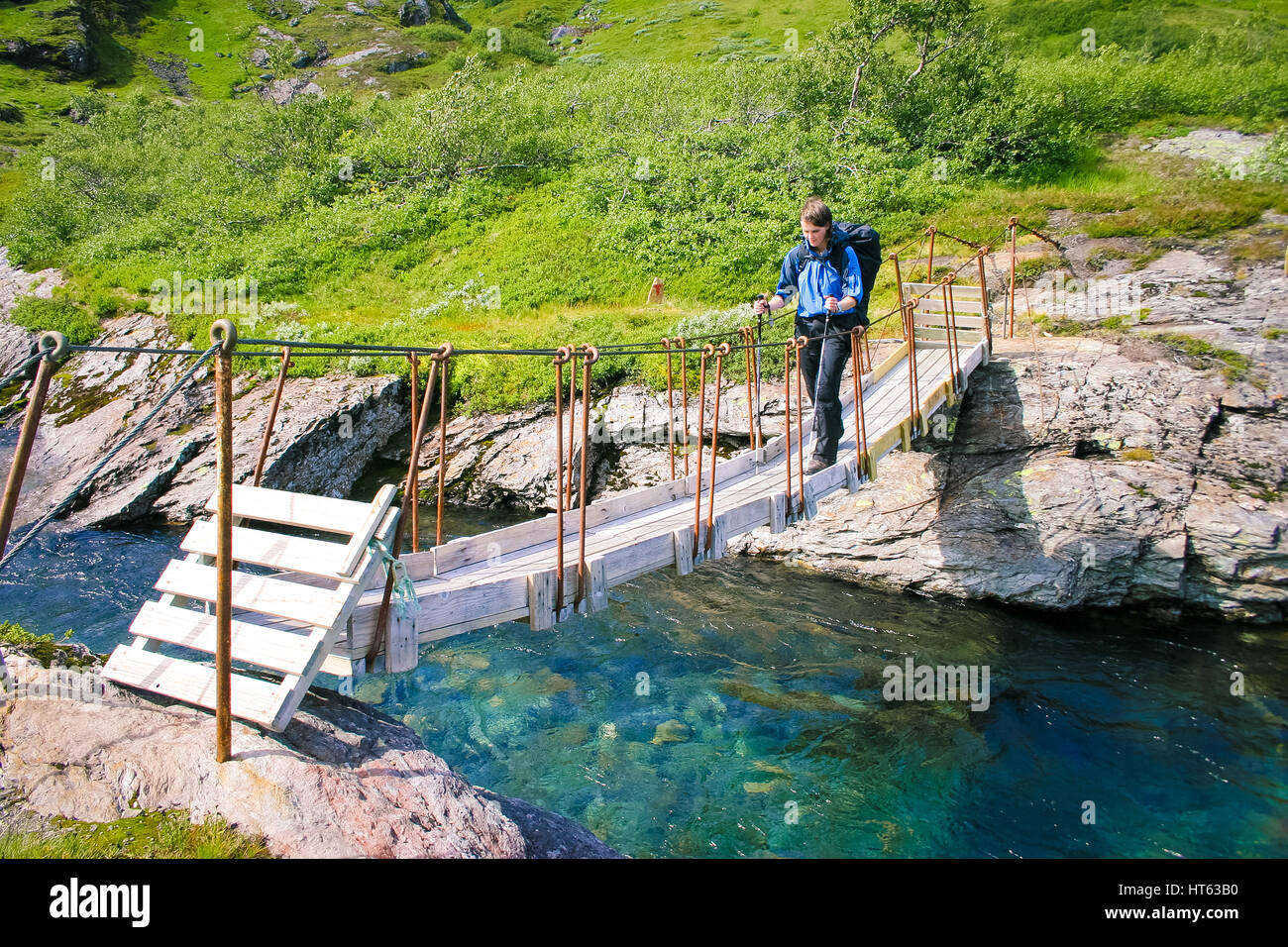 Young woman with backpack hiking across narrow wooden suspension bridge ...
