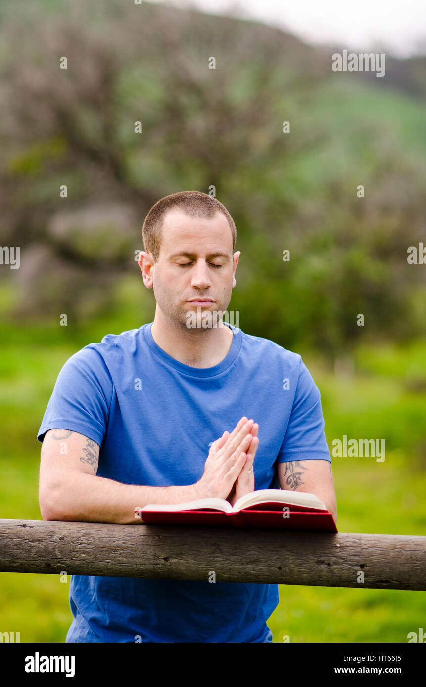 Man praying alone outside with hands together resting on an open book ...