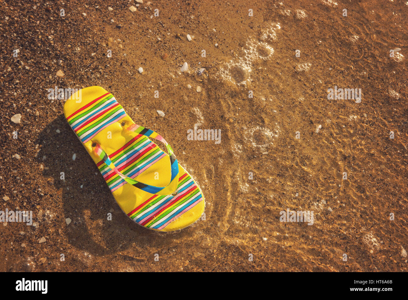 Top view of flip flop. Sand with transparent water. The lost shoe. Run ...