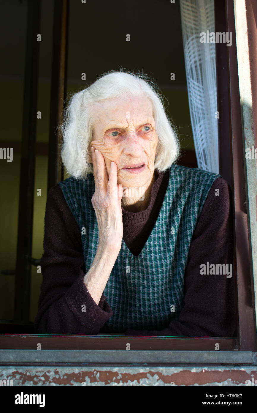 Senior woman looking through the house window Stock Photo - Alamy