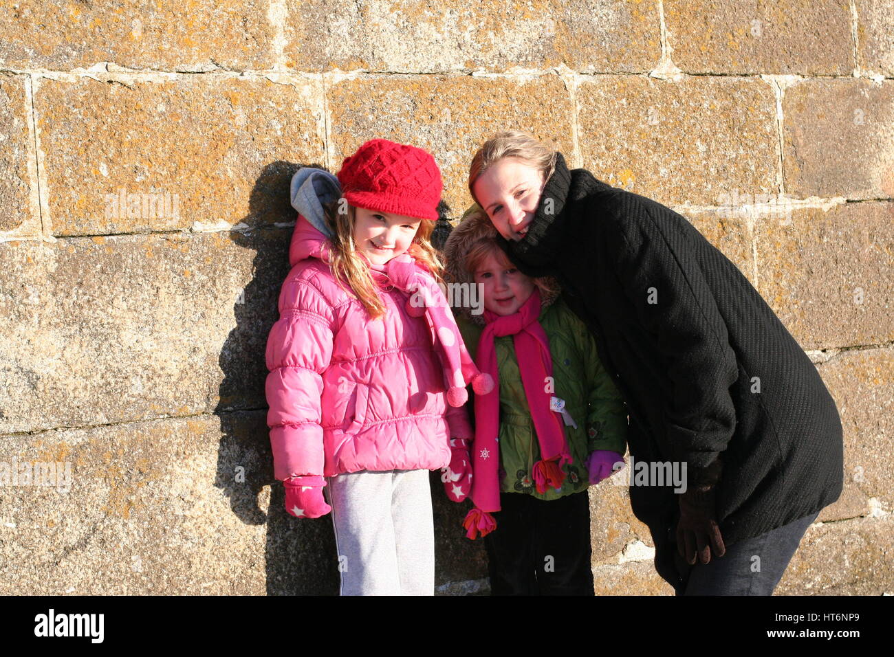 Little girls and their mum standing by a wall on a cold breezy day ...