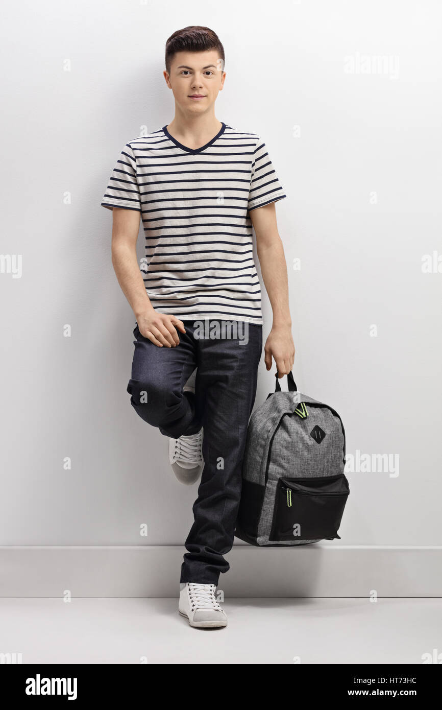 Full length portrait of a teenage boy holding a backpack leaning ...