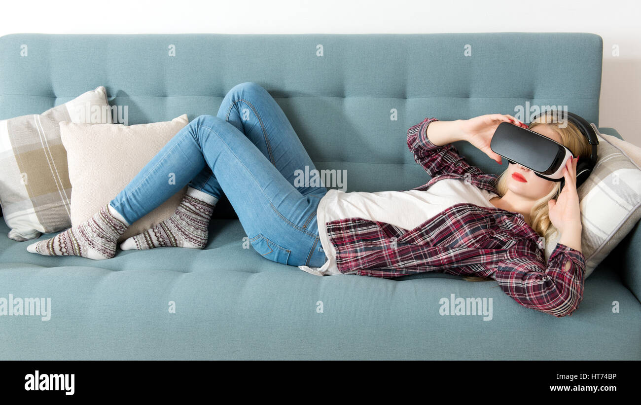 Attractive woman wearing virtual reality goggles lying on a couch ...