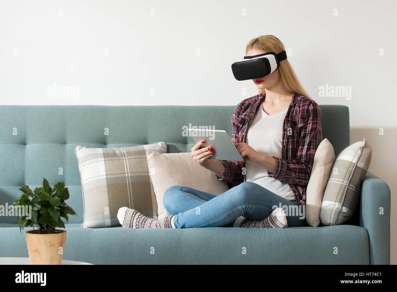 Attractive woman wearing virtual reality goggles sitting on a couch ...