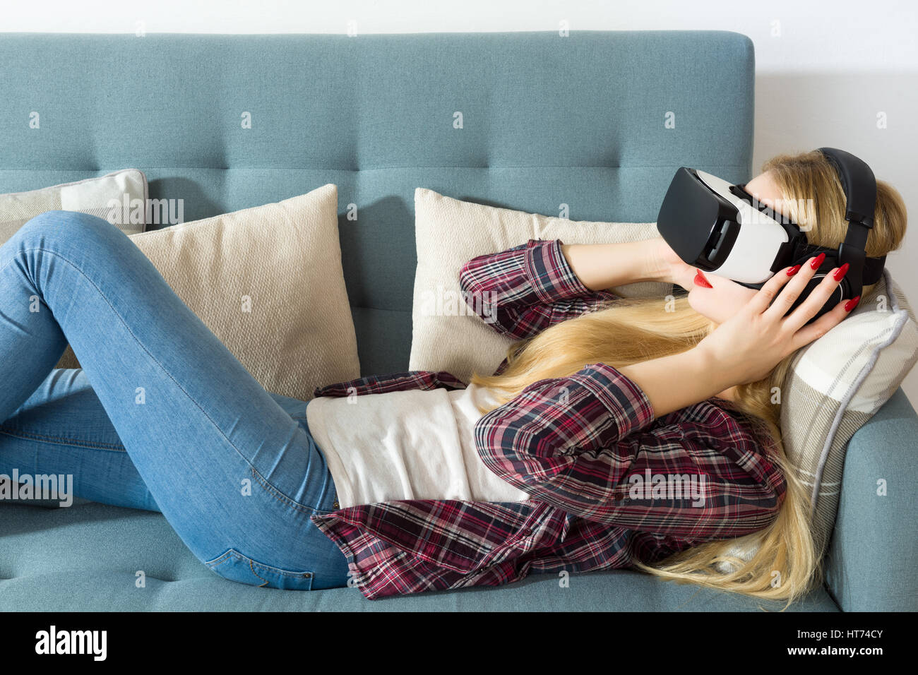 Attractive woman wearing virtual reality glasses lying on a couch ...