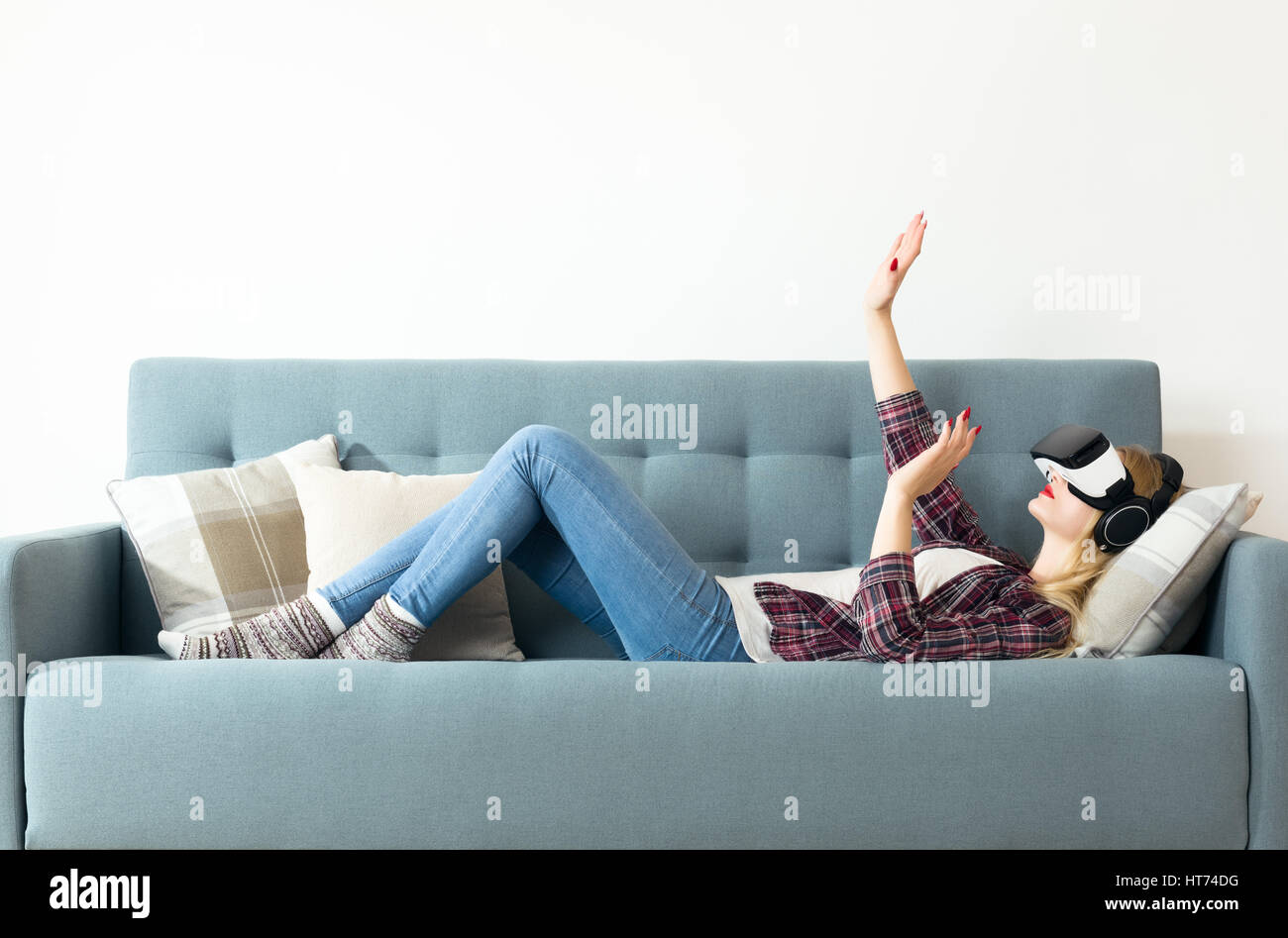 Attractive woman wearing virtual reality goggles lying on a couch ...