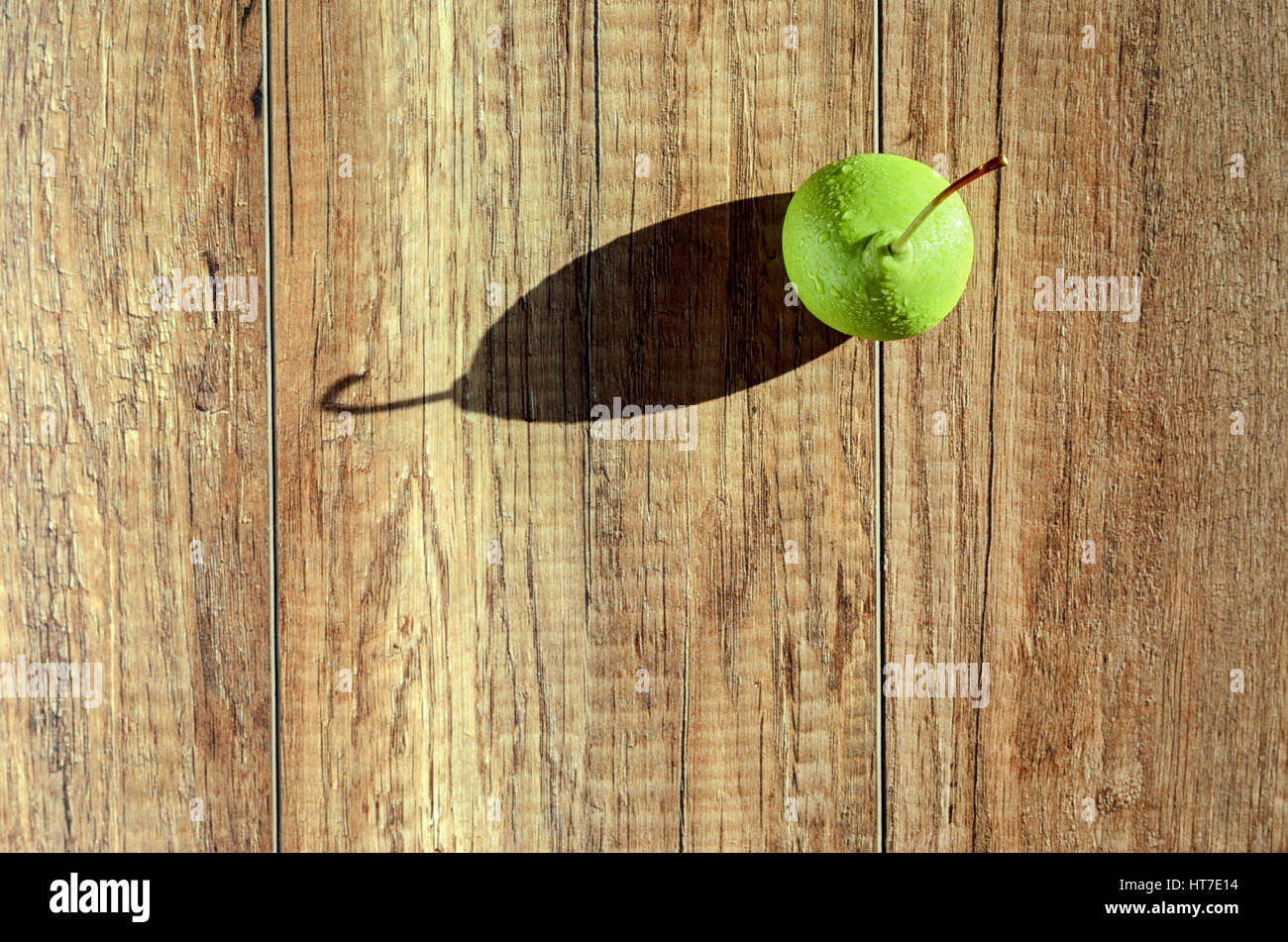 Alone juicy green pear with water drops cast a long shadow on wood ...