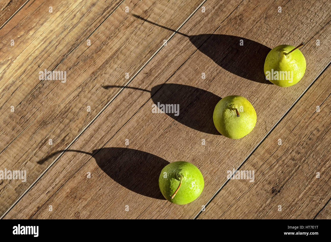 Three juicy green pears with water drops cast a long shadows on wood ...