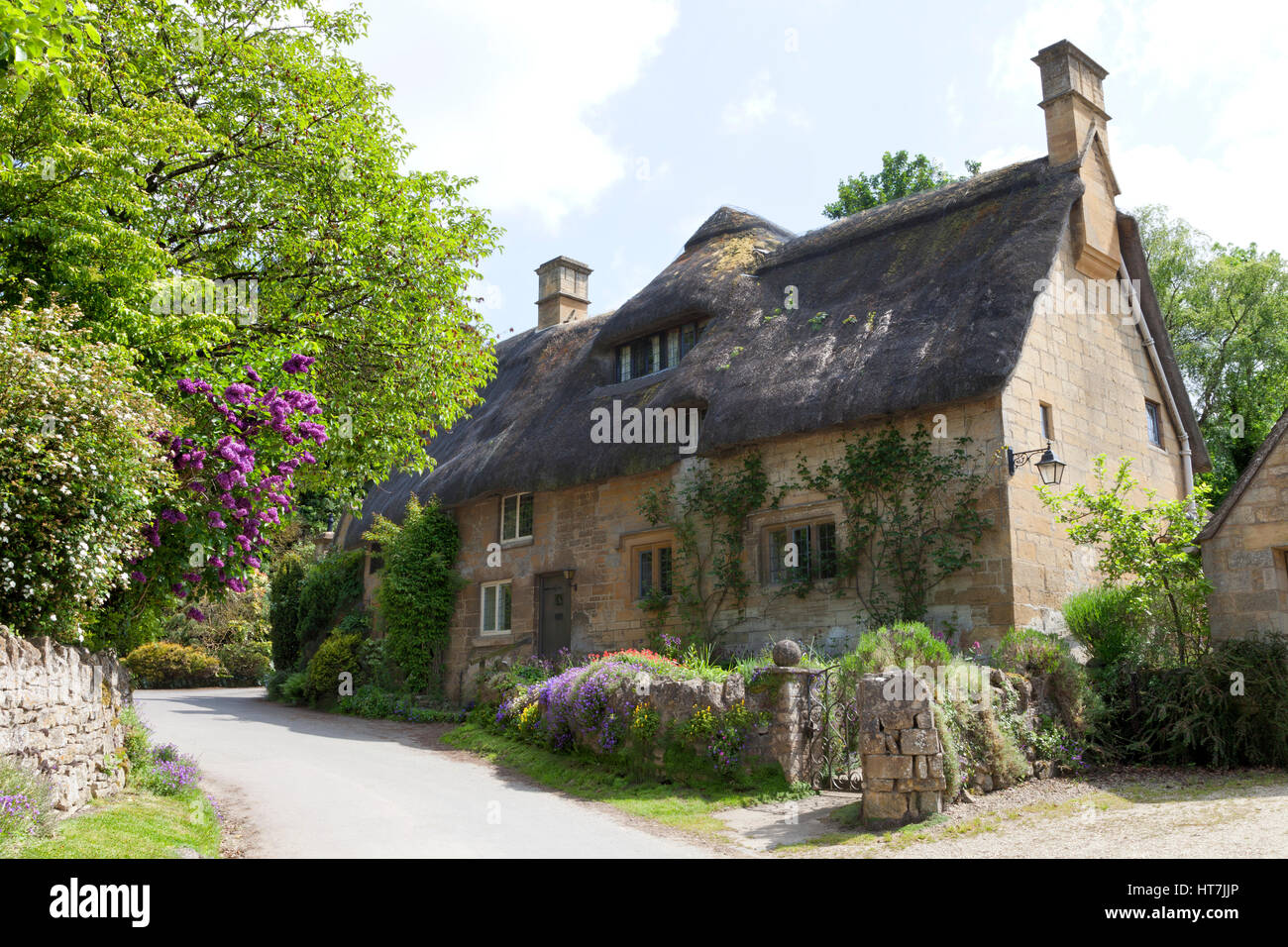 Thatched roof, stone cottage with flowering gardens, by a country road ...