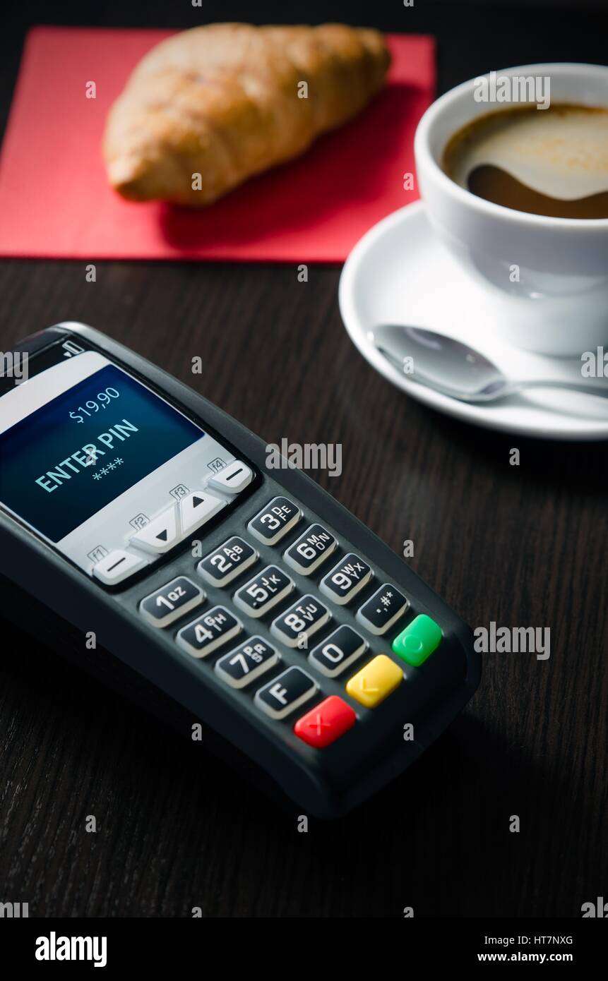 Payment terminal in restaurant. Croissaint and coffee in background ...