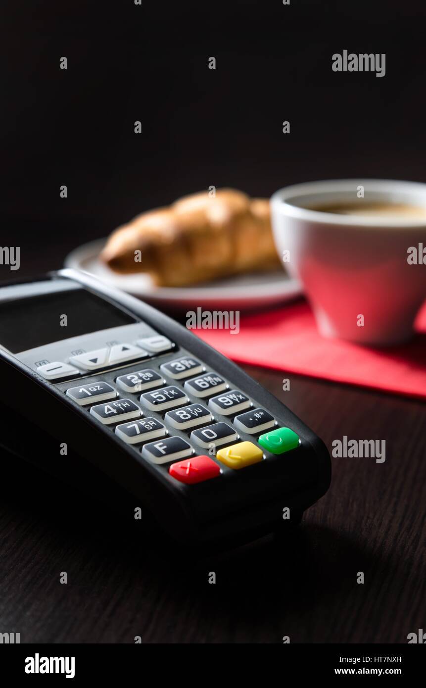 Payment terminal in restaurant. Croissaint and coffee in background ...