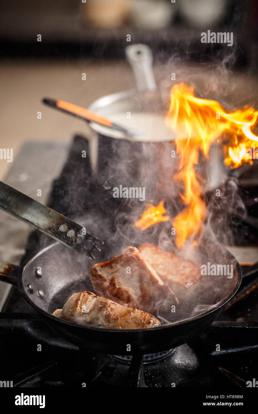 Chef cook in restaurant kitchen with pan over stove doing flambe Stock ...